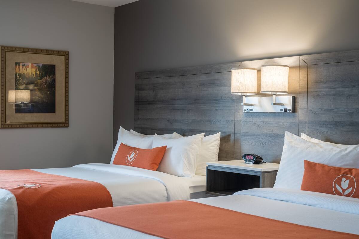 Quarto de hotel com duas camas, mesa de cabeceira, abajur e um quadro pendurado na parede.