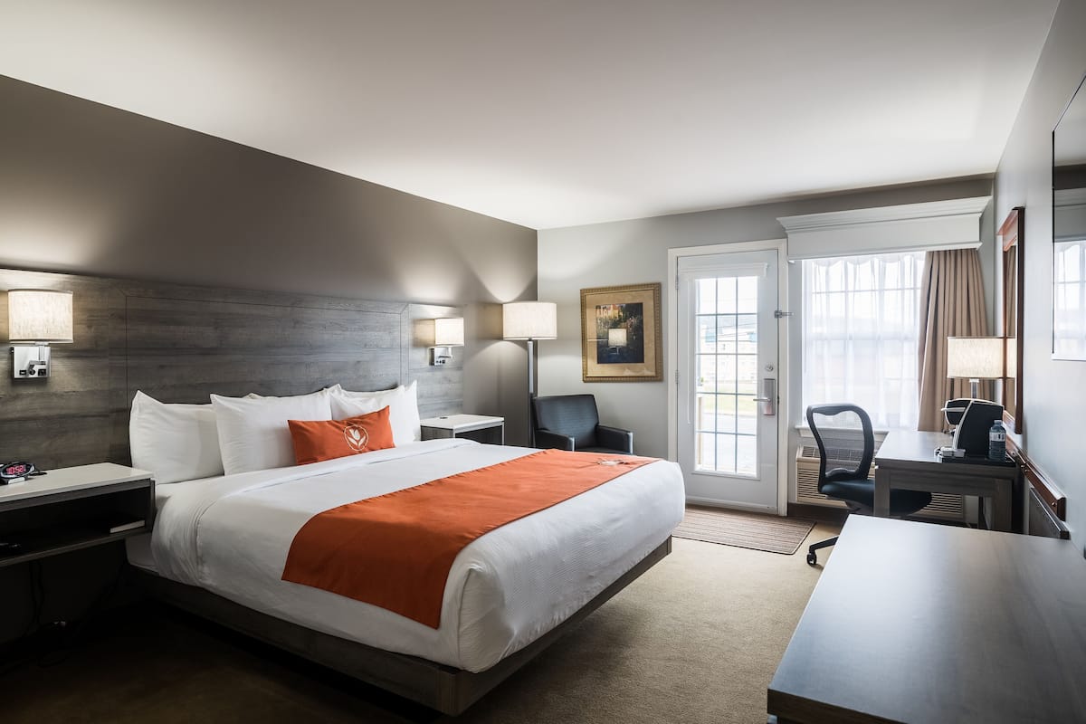 Quarto de hotel com cama, escrivaninha, cadeira e porta para uma varanda.