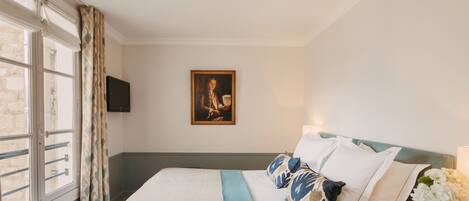 Quarto bem arrumado com uma cama, um quadro na parede e uma janela com cortinas.