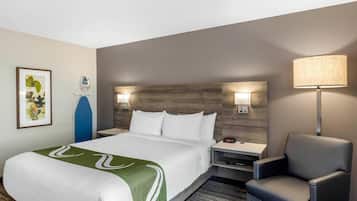 Quarto de hotel com cama, mesas de cabeceira, abajur, cadeira e quadro na parede.