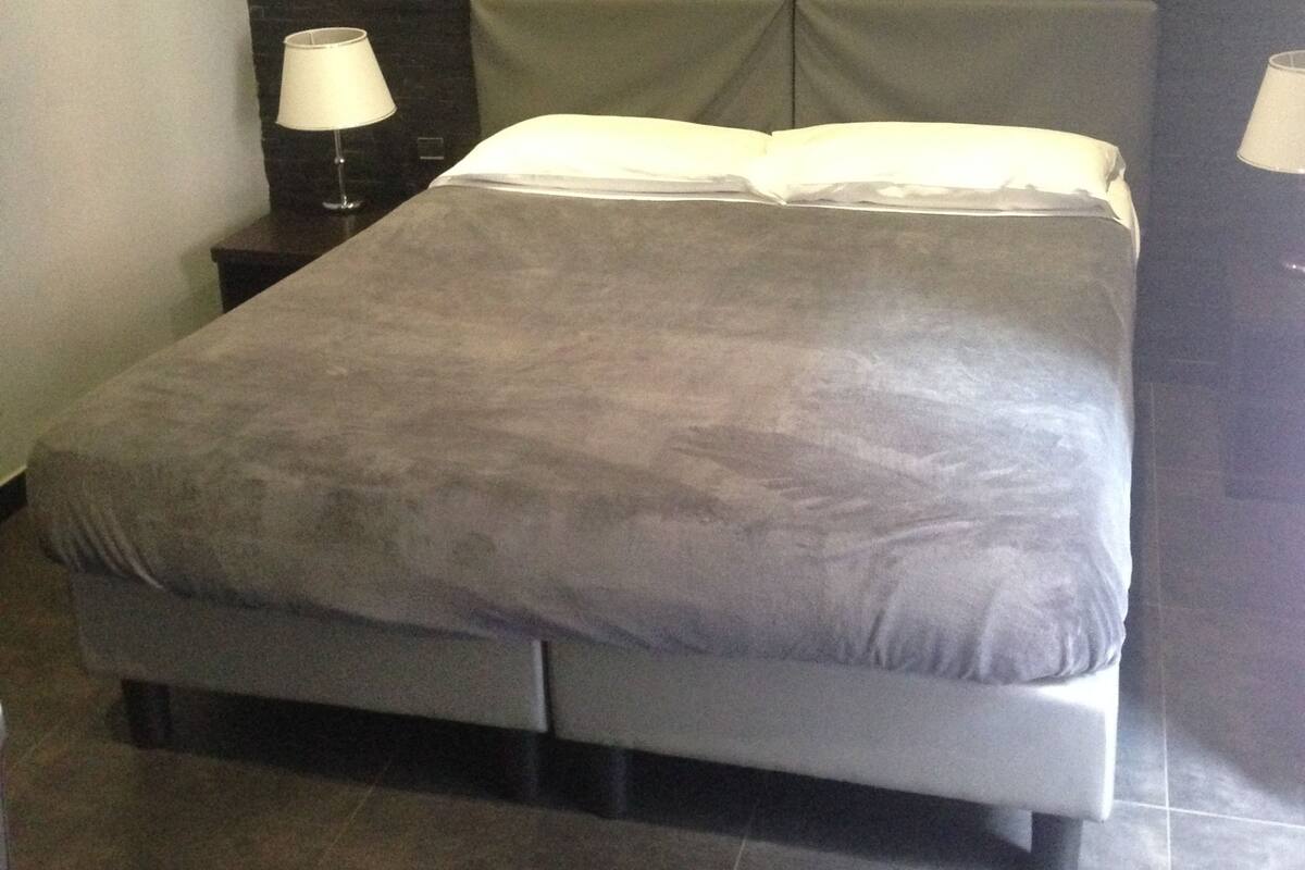 Quarto moderno com uma cama grande, duas luminárias de cabeceira e uma parede escura.