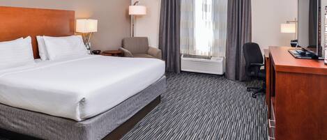 Quarto de hotel com uma cama grande, uma escrivaninha, uma cadeira, um abajur e uma televisão.