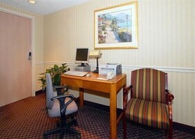 Quarto de hotel com uma escrivaninha, poltrona listrada, computador e um quadro na parede.