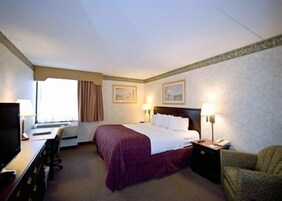 Quarto de hotel com cama, escrivaninha, cadeira e duas luminárias de cabeceira.