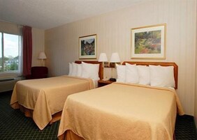 Quarto de hotel com duas camas, janela com vista e duas pinturas na parede.