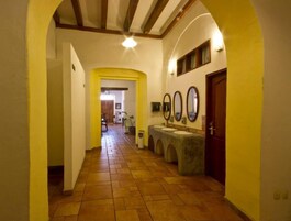 Um corredor com piso ladrilhado, um arco amarelo e uma fileira de pias com espelhos.