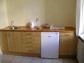 Uma cozinha compacta com pia, chaleira, pequeno frigorífico e armários de madeira.