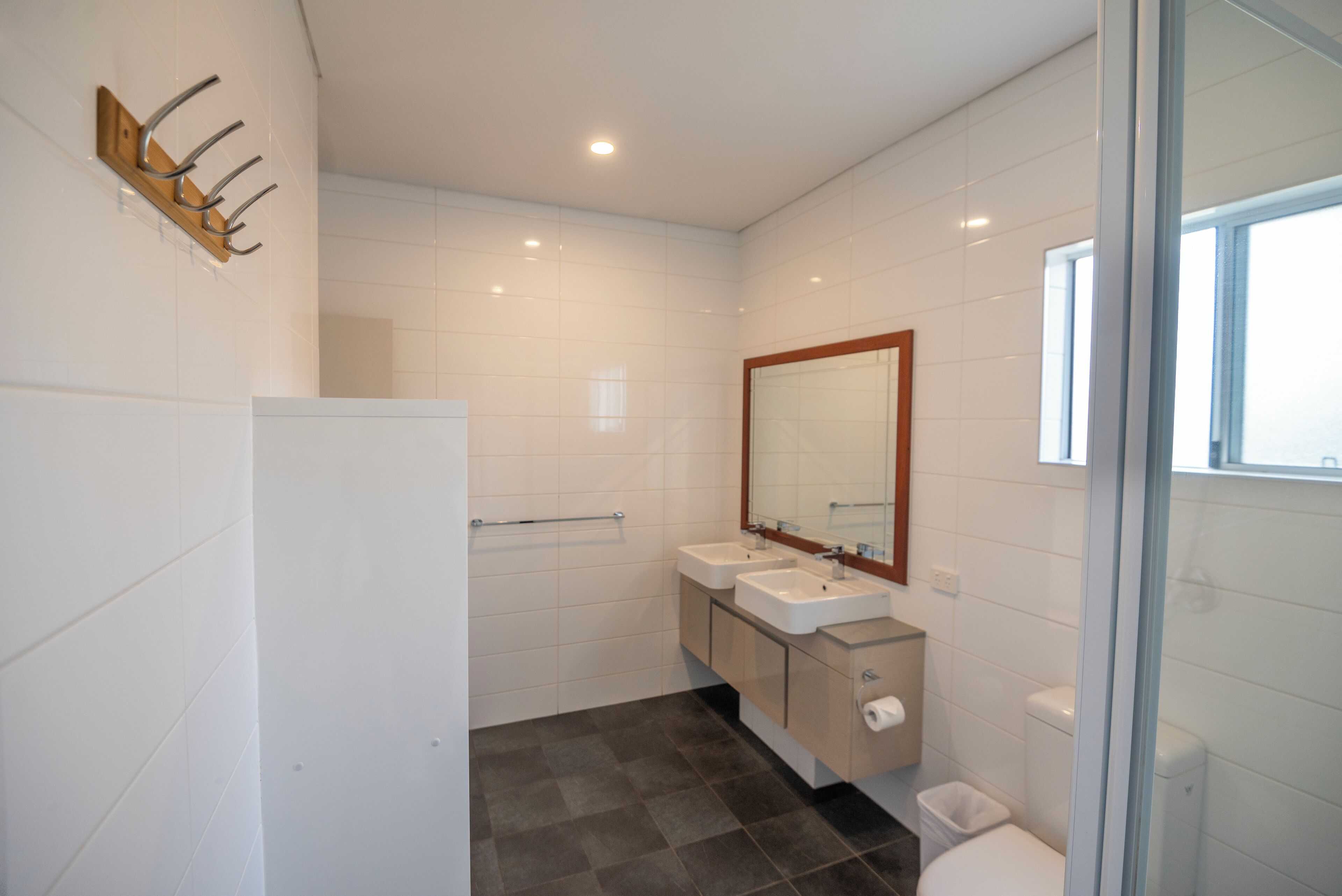 Casa de banho com azulejos brancos, duas lavatórios, um espelho e zona de duche.