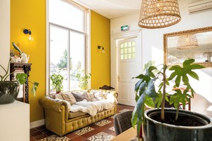 Quarto com parede amarela, porta branca, sofá e planta em vaso.