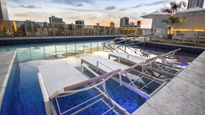 Piscina no terraço com espreguiçadeiras e vista para o horizonte da cidade.