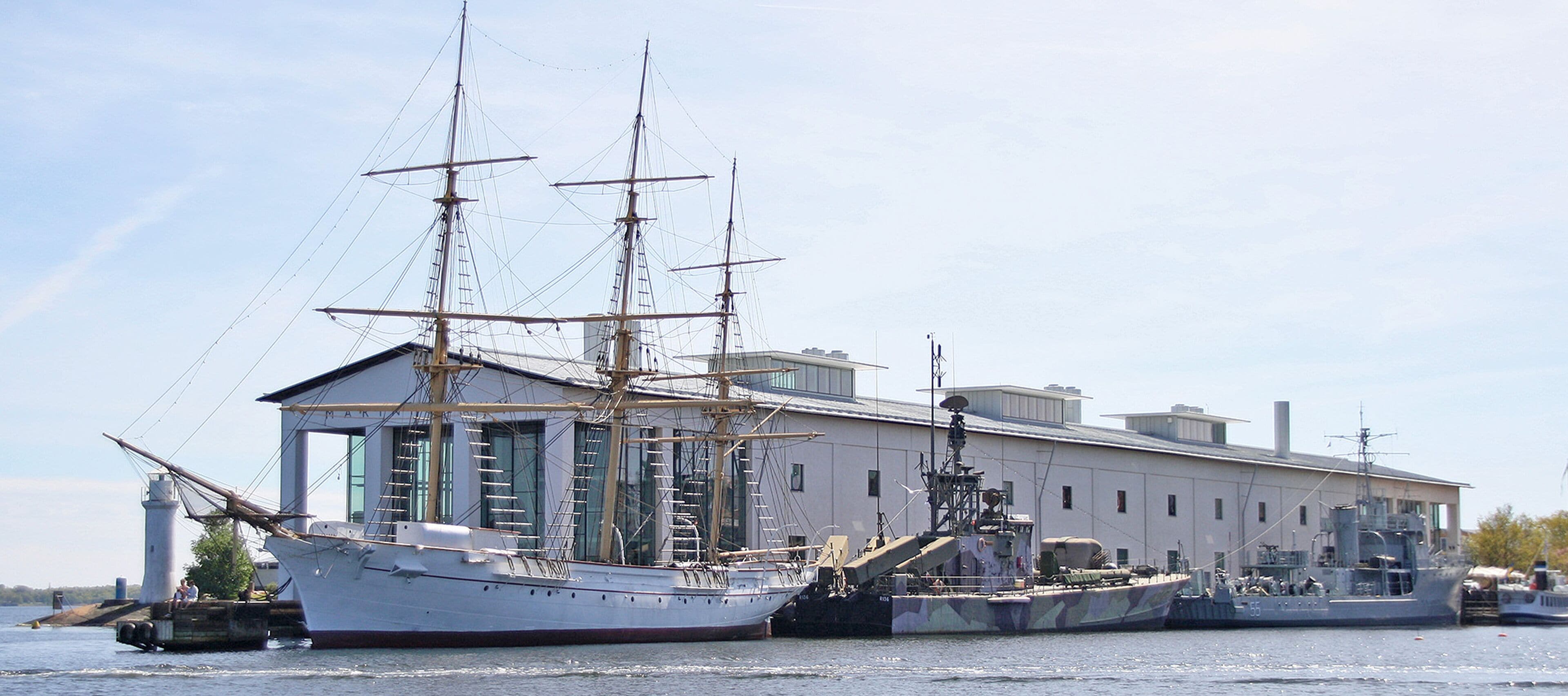 Um grande navio à vela histórico atracado em um estaleiro moderno.