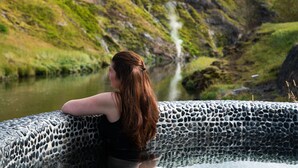 Uma pessoa sentada perto de uma fonte de água, com uma paisagem rochosa ao fundo.