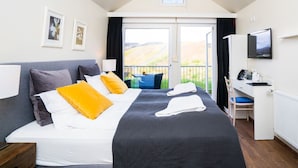 Quarto de hotel com uma cama grande, uma escrivaninha, uma cadeira, uma televisão e varanda com vista.