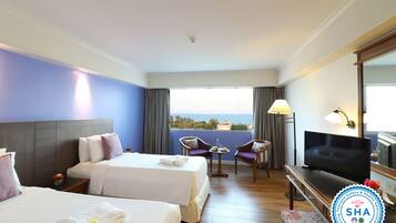 Quarto de hotel com duas camas, televisão, uma mesinha com abajur e varanda com vista.