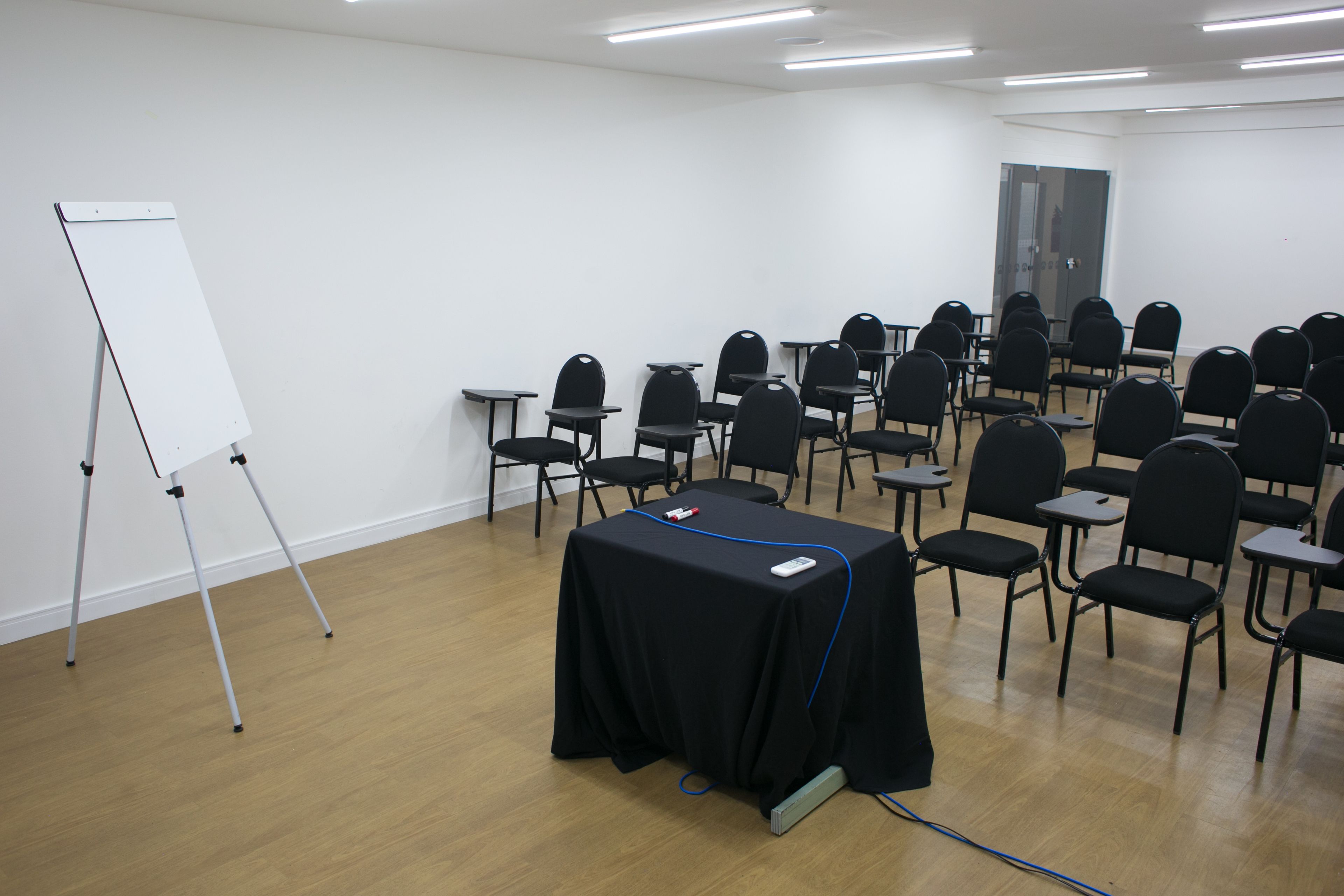Sala de conferências com quadro branco, mesas e cadeiras dispostas para uma reunião.