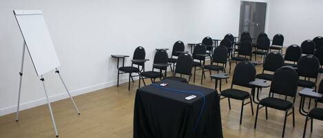 Sala de conferências com quadro branco, mesas e cadeiras dispostas para uma reunião.