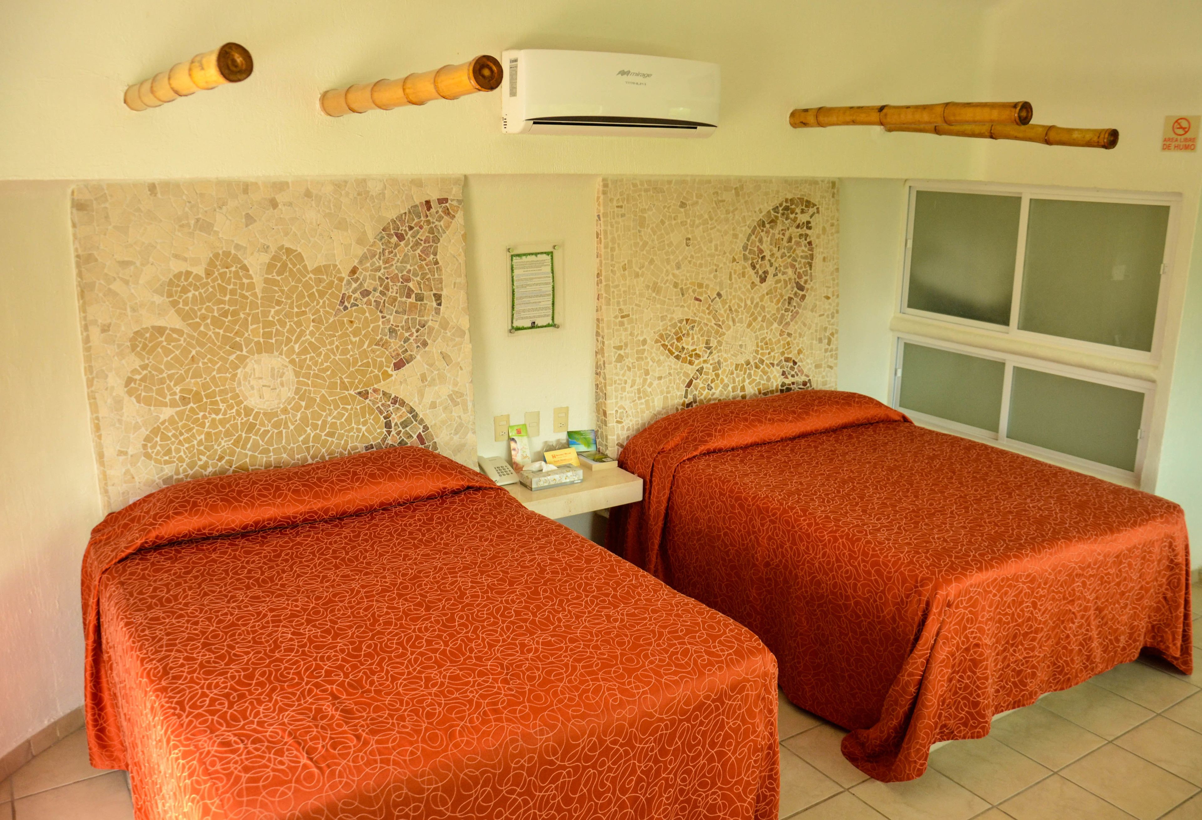 Quarto com duas camas, ar-condicionado, janela e parede com design em mosaico.