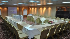 Uma sala de conferências com uma mesa comprida, cadeiras e uma tela de projeção.