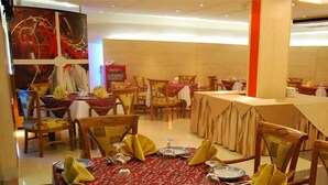 Restaurante com cadeiras e mesas de madeira, área de buffet e balcão com um atendente.