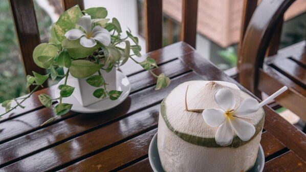 Uma mesa de madeira com um bolo branco coberto por uma flor branca e um canudo, além de uma planta em vaso com folhas verdes.