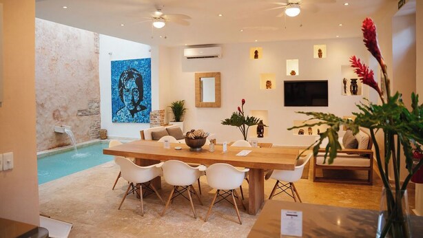 Uma sala de estar moderna com área de jantar, piscina e uma grande obra de arte na parede.