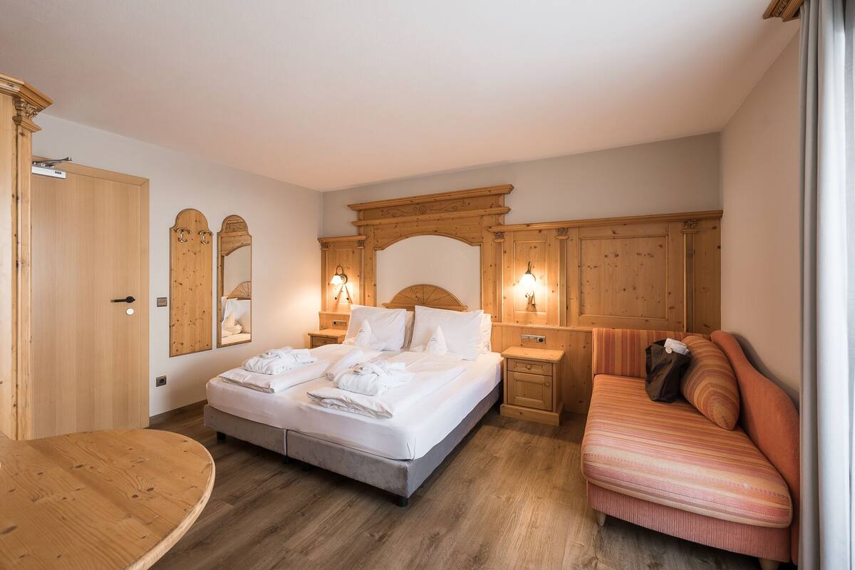 Um quarto com uma cama, uma mesa de cabeceira de madeira, um sofá e um guarda-roupa de madeira.
