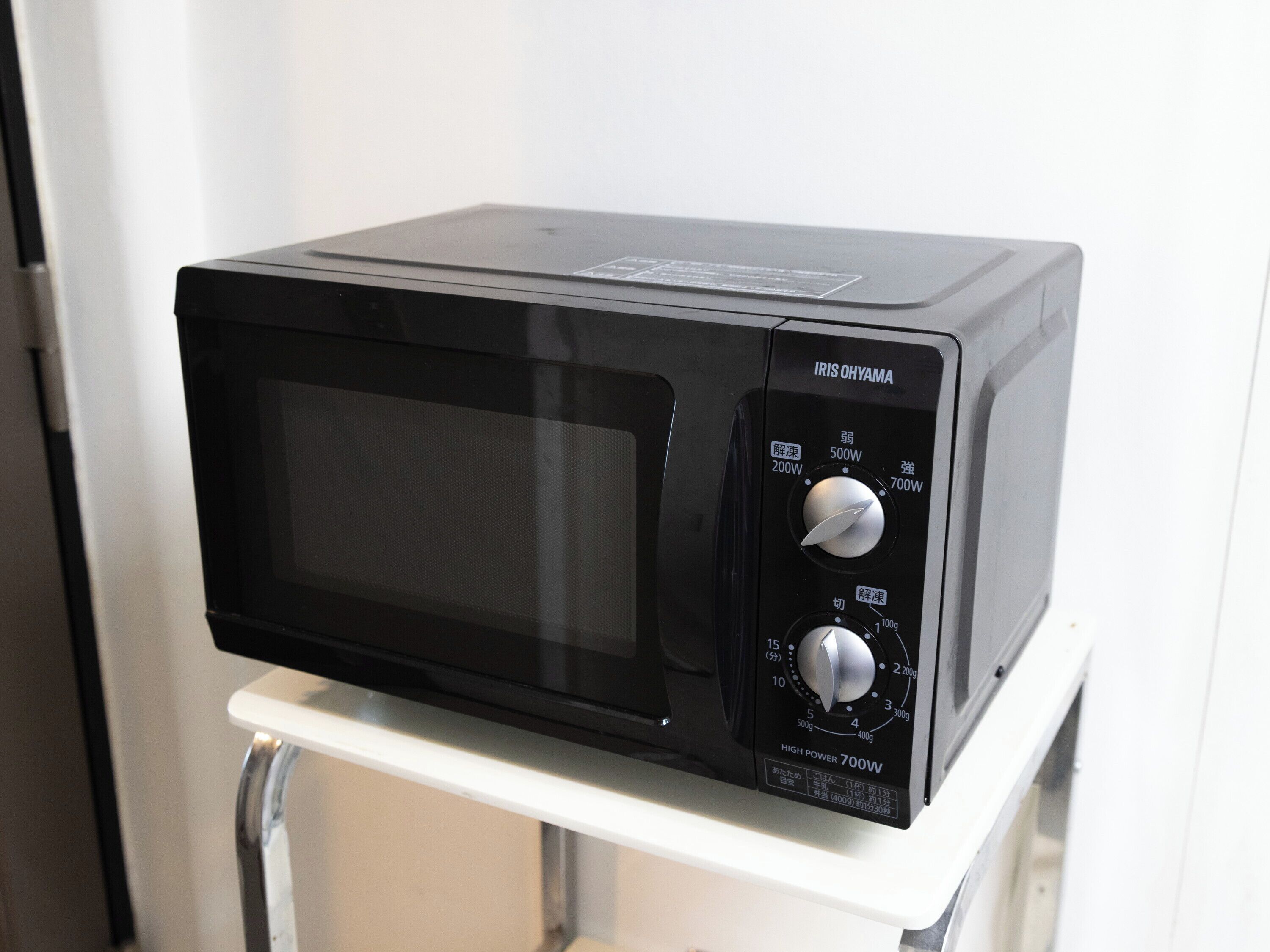 Um forno de micro-ondas preto com visor digital e botões de controle sobre uma prateleira branca.