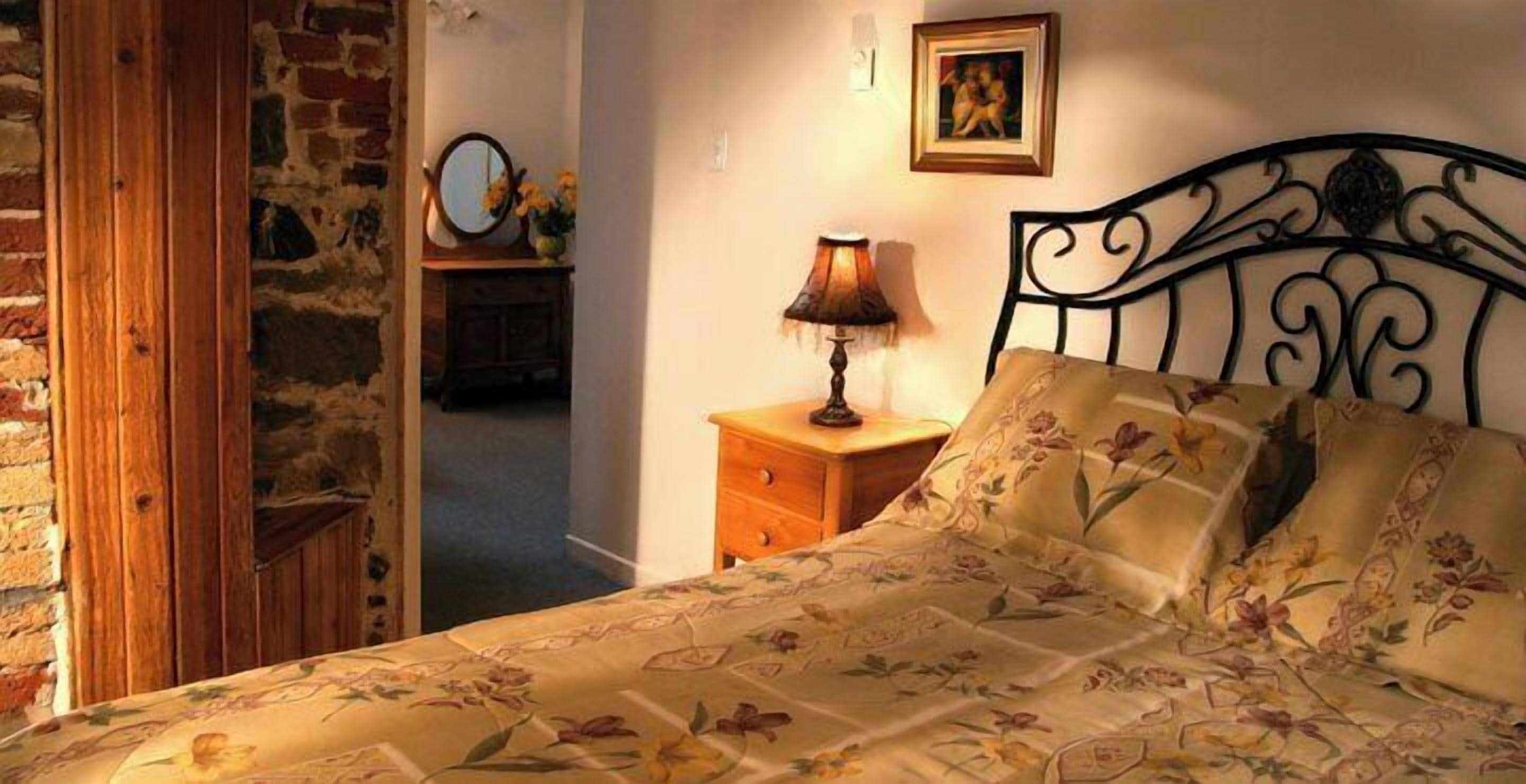 Quarto com cama, mesa de cabeceira, abajur, espelho e um quadro na parede.