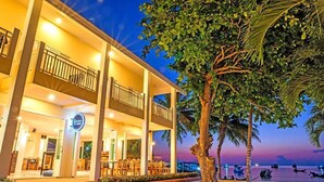 Um hotel com estrutura em dois andares, área de estar externa e vista para a praia com barcos.