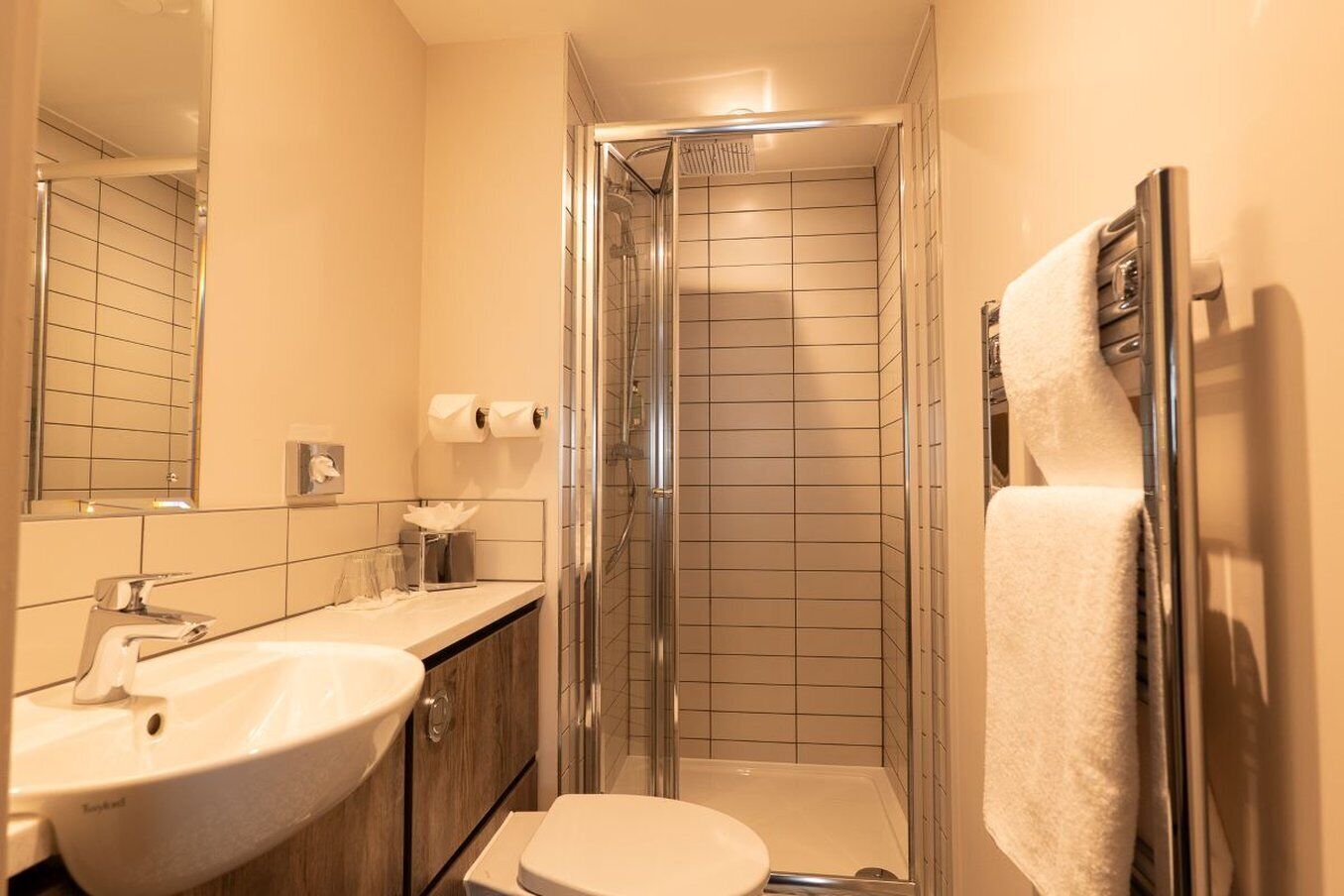 Uma casa de banho moderna com cabine de duche em vidro, lavatório com espelho e sanita.