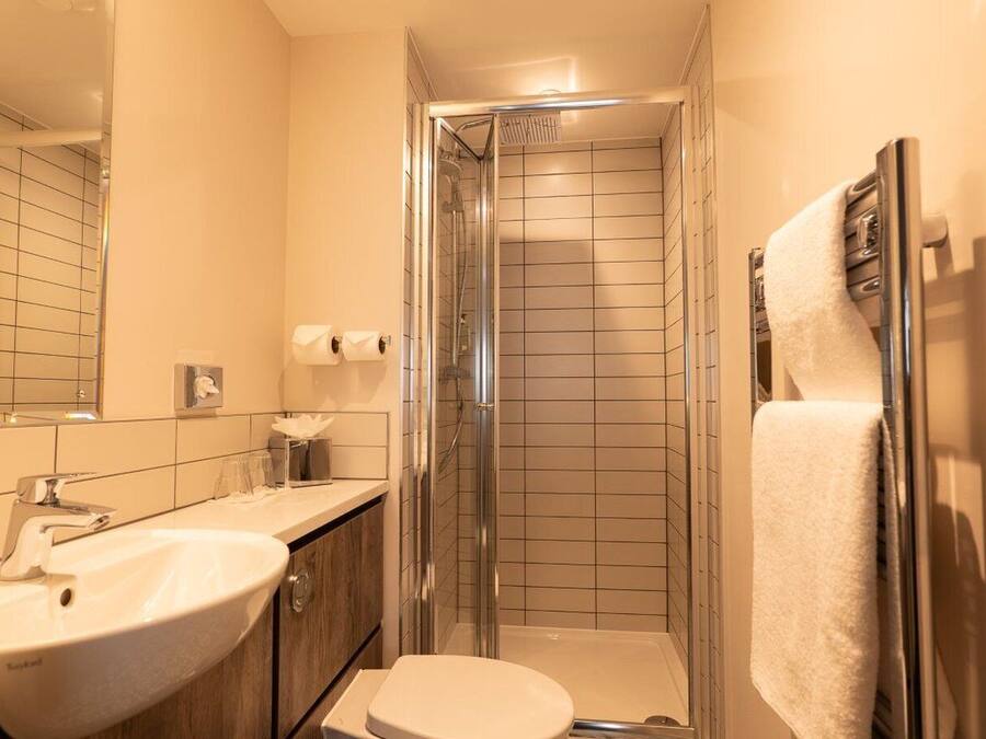 Uma casa de banho moderna com cabine de duche em vidro, lavatório com espelho e sanita.