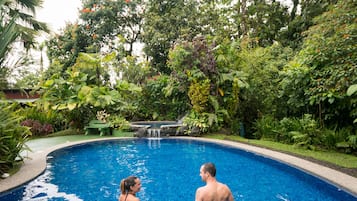 Piscina rodeada por vegetação exuberante e uma cascata.