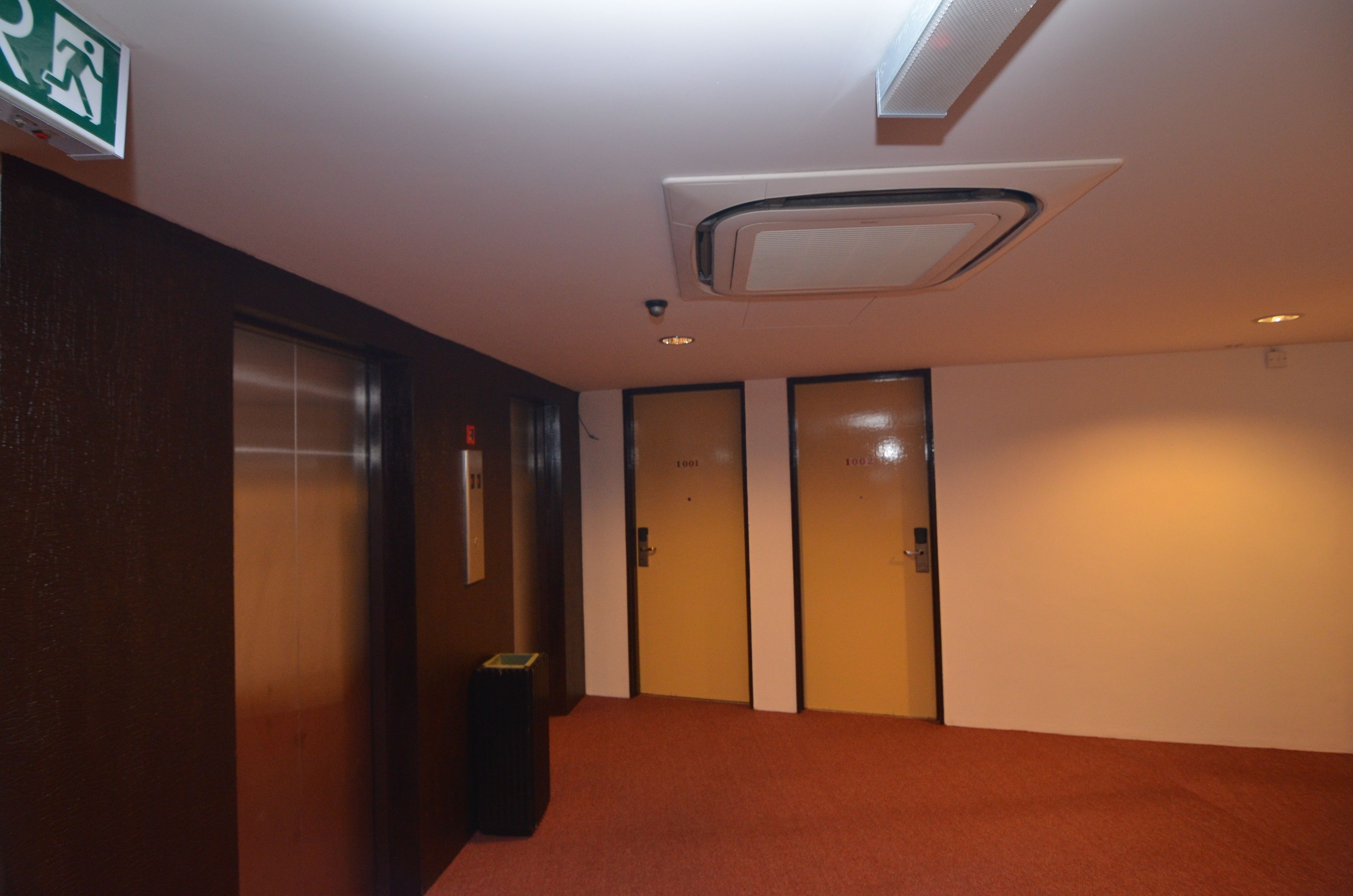 Um corredor com três portas, uma lixeira e uma placa de saída de emergência.
