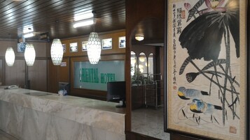 Uma área de recepção com balcão, relógio e uma placa que diz "ORIENTAL HOTEL".