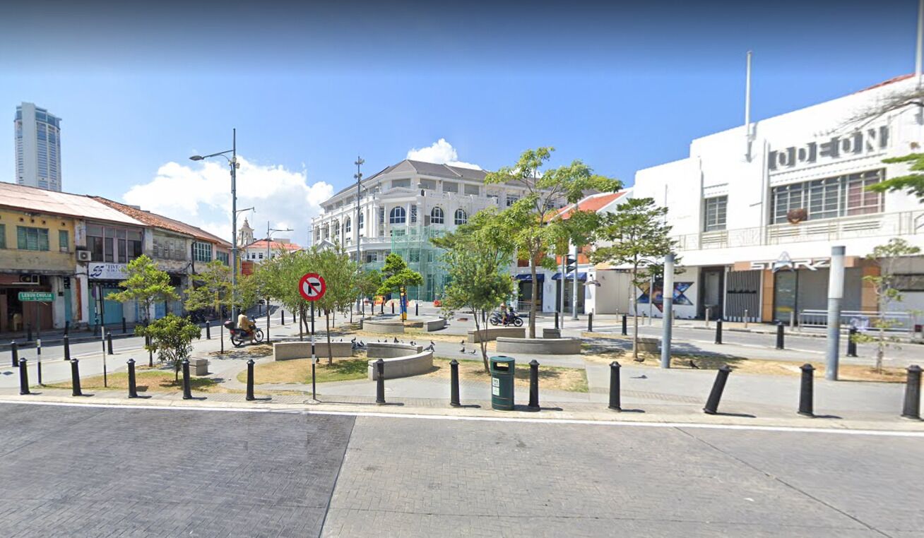 Uma praça para pedestres com placa de proibido estacionar, cercada por edifícios com estabelecimentos comerciais.