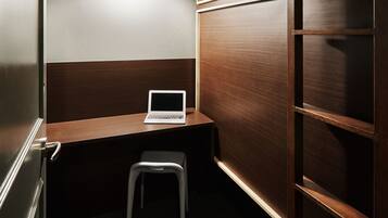 Um quarto pequeno e com pouca luz, com uma escrivaninha de madeira, um laptop e um candeeiro suspenso.