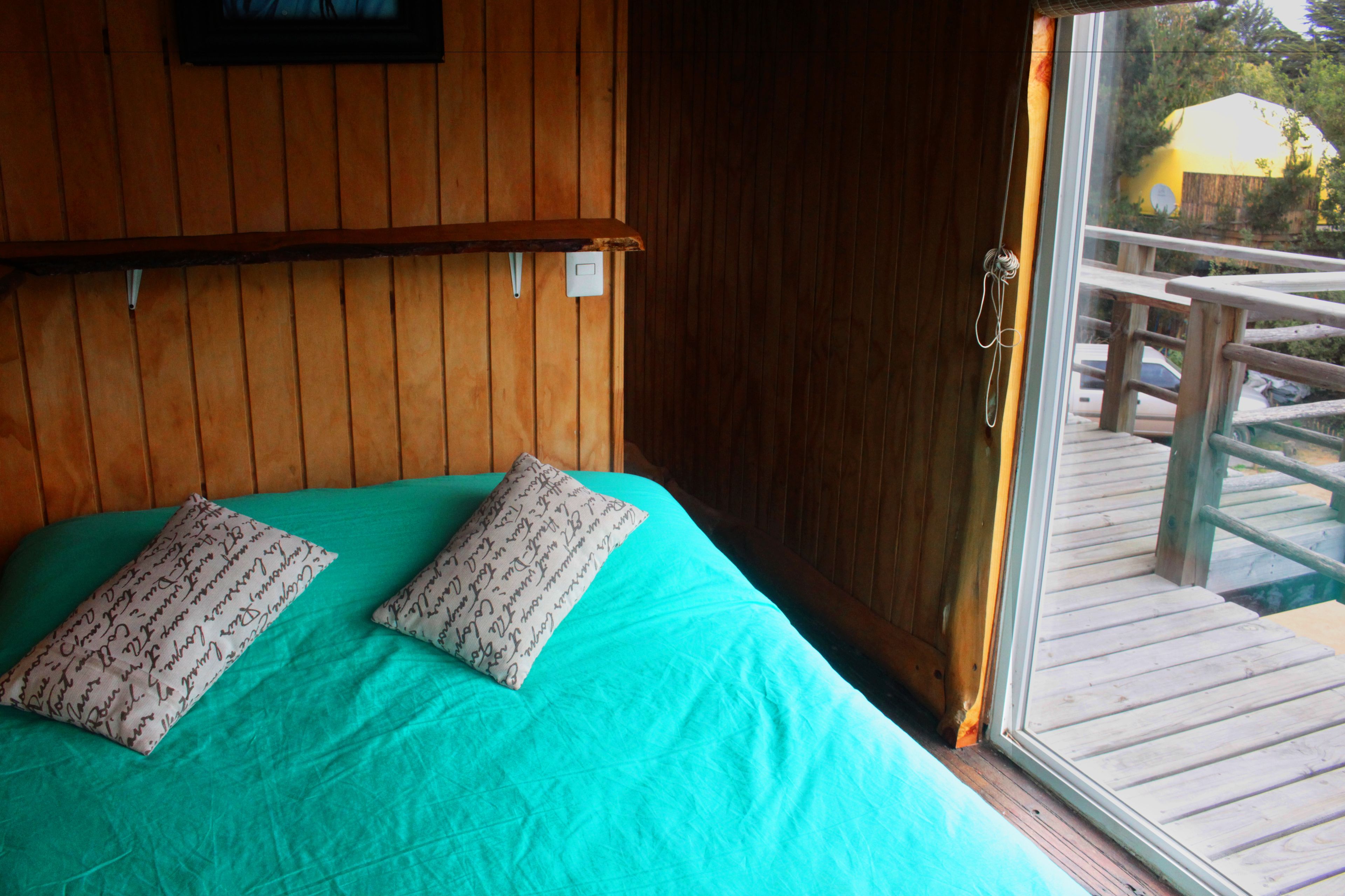 Quarto com cama, paredes de madeira, uma janela e vista para um deck.