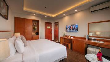 Quarto de hotel com cama, escrivaninha, televisão e pequena mesa com garrafa e copos.
