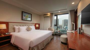 Quarto de hotel com uma cama grande, escrivaninha, cadeira, televisão e vista para a paisagem urbana.