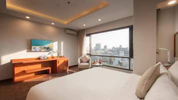 Quarto de hotel com uma cama grande, escrivaninha, cadeira, televisão e vista para a cidade.