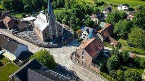 Vista aérea de uma aldeia com uma igreja destacada, casas residenciais e campos ao redor.