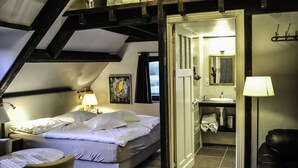Quarto com cama, mesas de cabeceira, uma cadeira, escrivaninha e banheiro com pia, espelho e porta-toalhas.