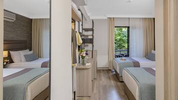Quarto de hotel com duas camas, uma pequena escrivaninha com um vaso de flores e vista para o verde lá fora.