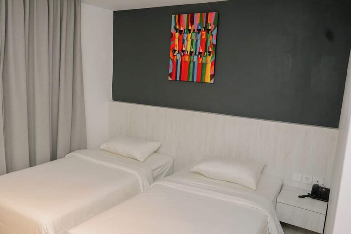 Quarto de hotel com duas camas, mesa de cabeceira com telefone e pintura abstrata colorida na parede.