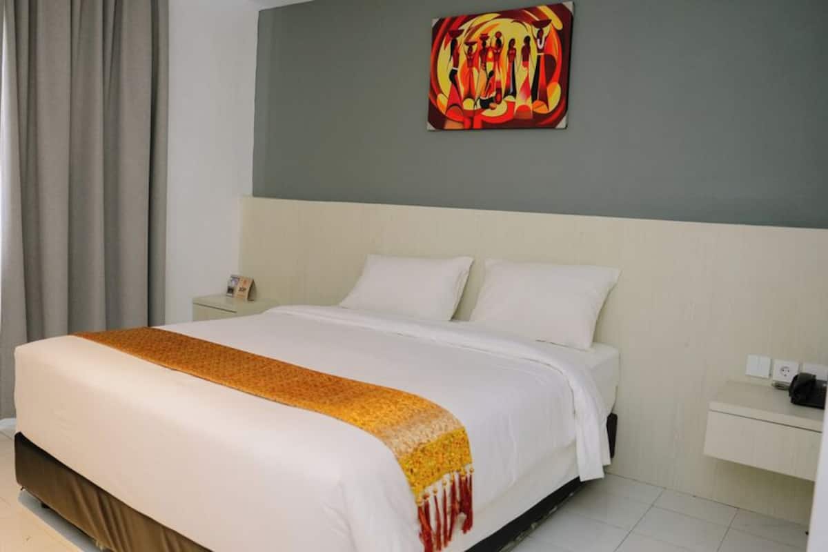 Quarto de hotel com cama, mesa de cabeceira, um quadro na parede e janela com cortinas.