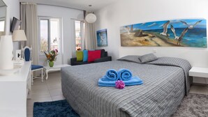 Quarto de hotel moderno com uma cama grande, uma escrivaninha, uma cadeira e um quadro de gaivotas na parede.