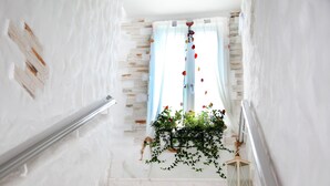 Uma escadaria com paredes brancas, um corrimão de madeira e uma planta pendente com flores vermelhas.