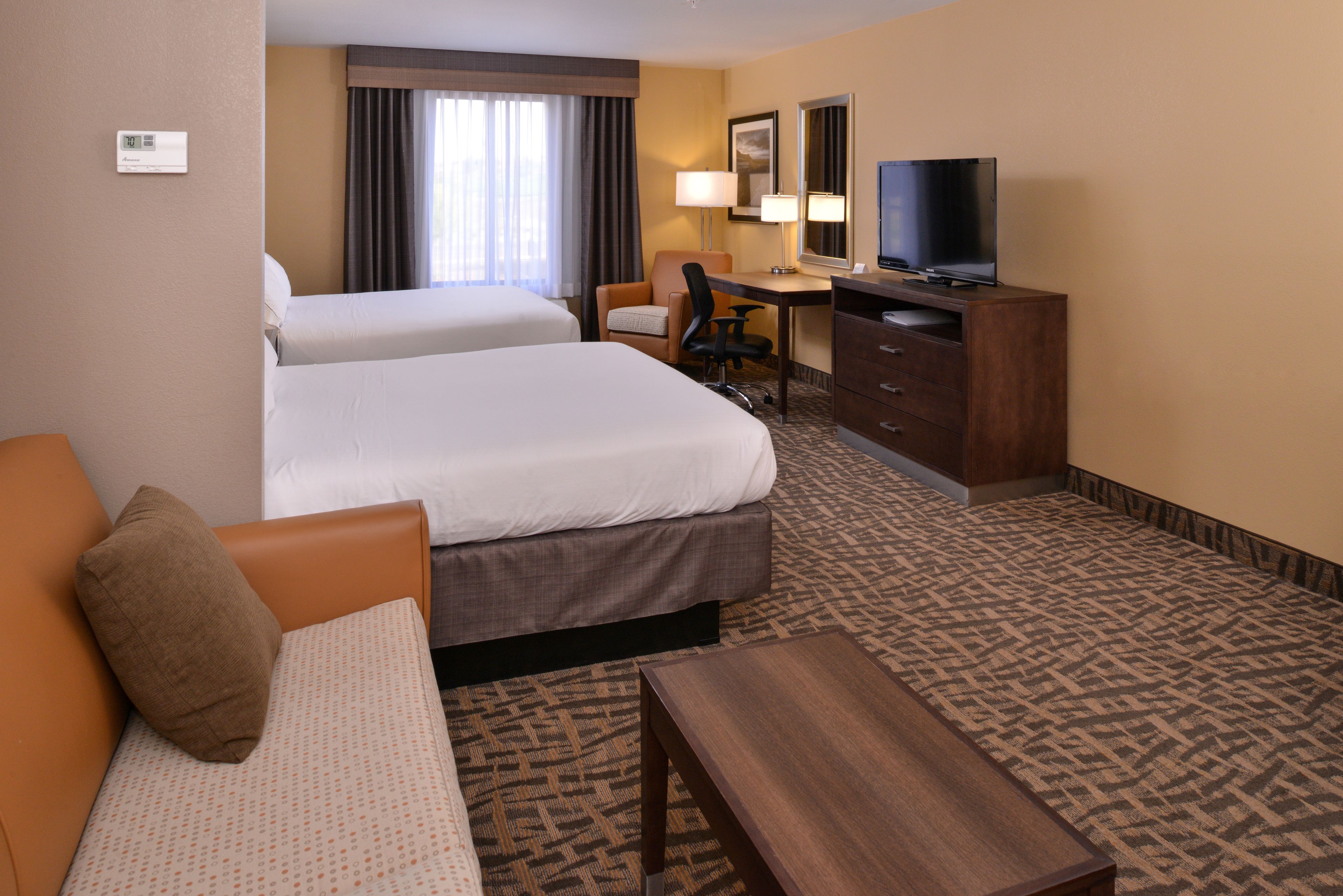 Quarto de hotel com duas camas, uma escrivaninha, televisão e um espaço para sentar.