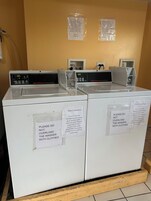 Uma fileira de máquinas de lavar industriais brancas, com instruções coladas.