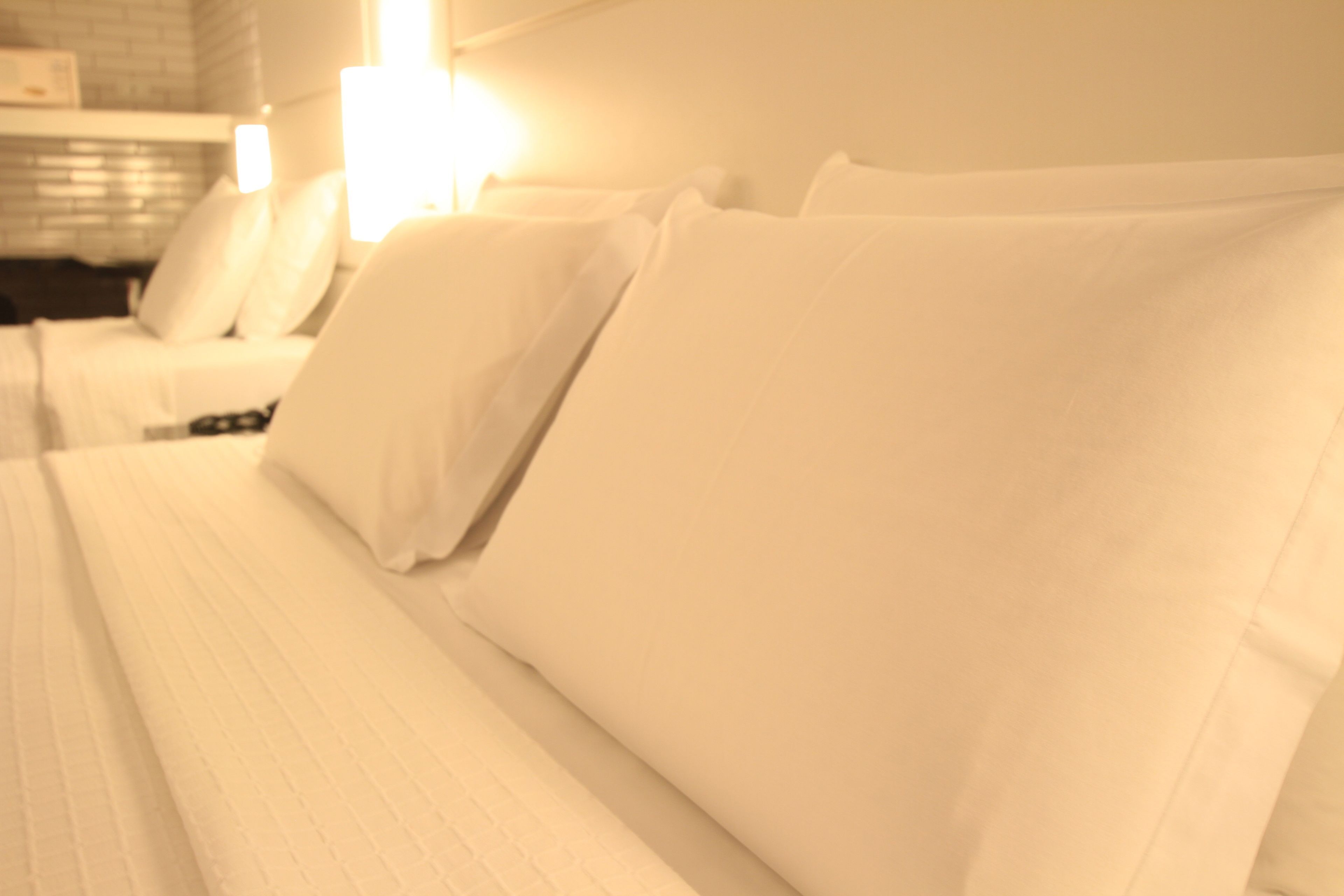 Quarto de hotel com cama, almofadas e mesa de cabeceira com abajur.